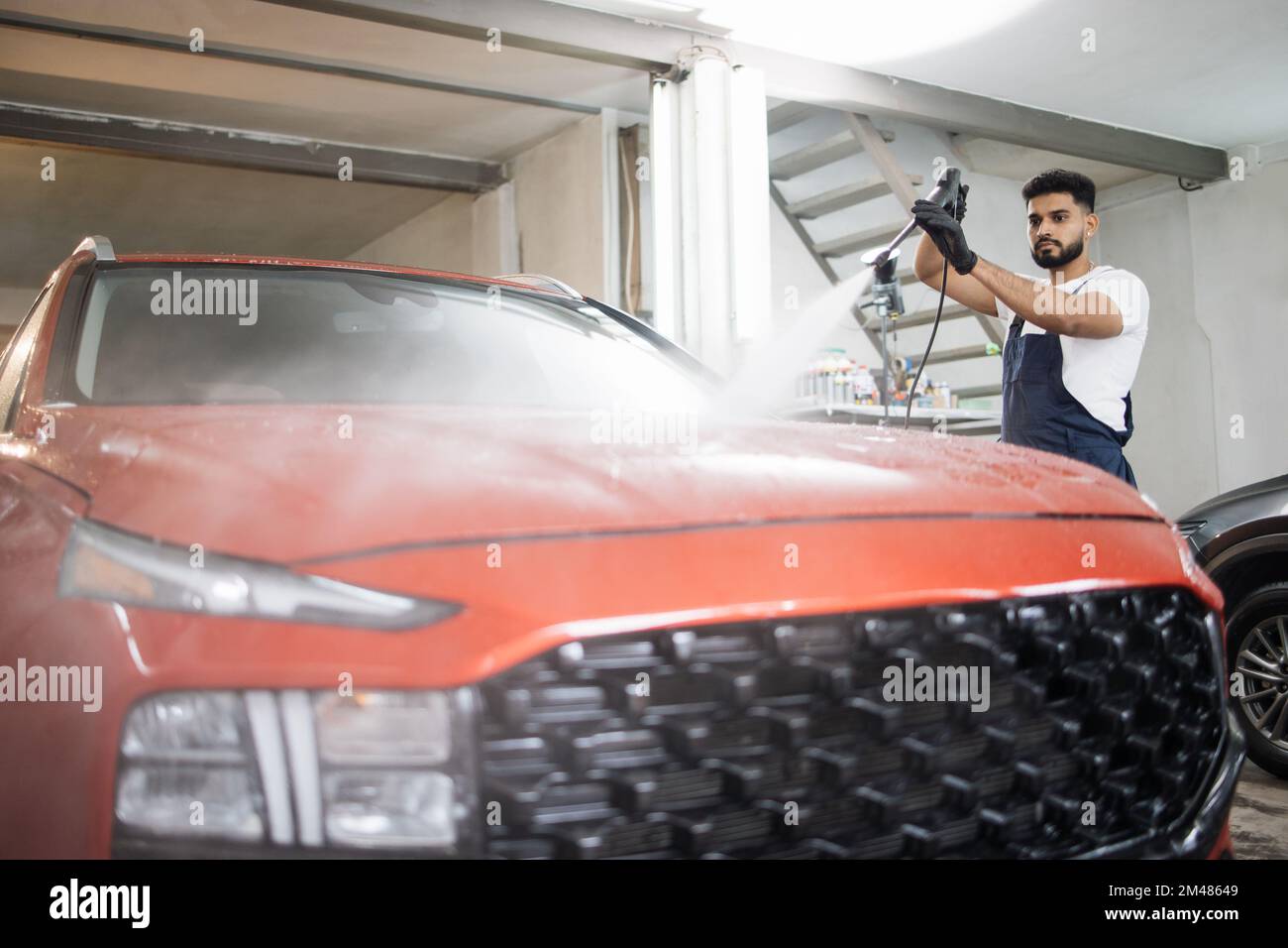 Cleaning car using high pressure water gun. Handsome young bearded man ...