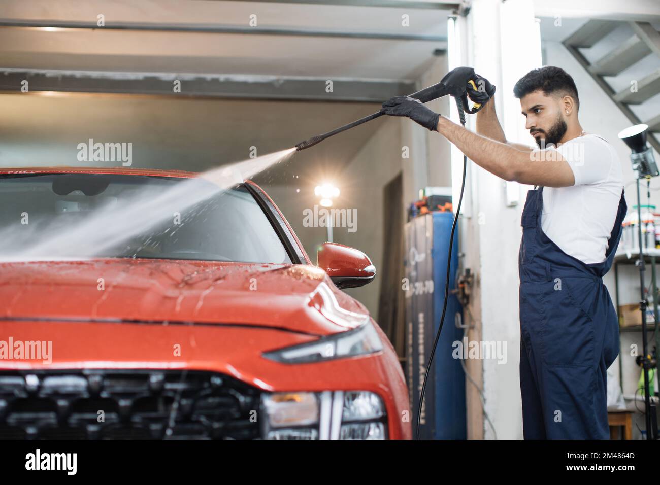 Cleaning car using high pressure water gun. Handsome young bearded man ...