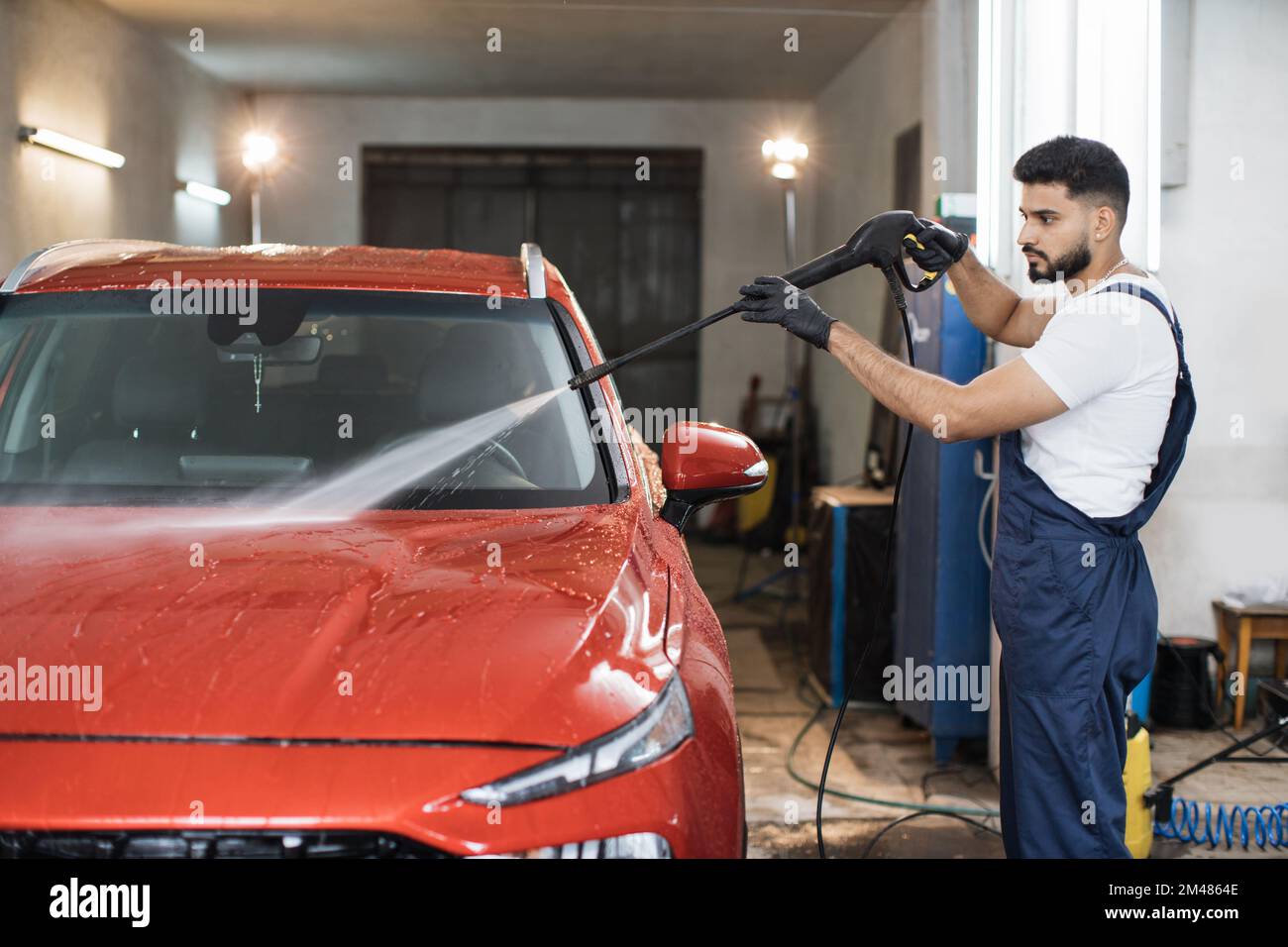 Cleaning car using high pressure water gun. Handsome young bearded man ...