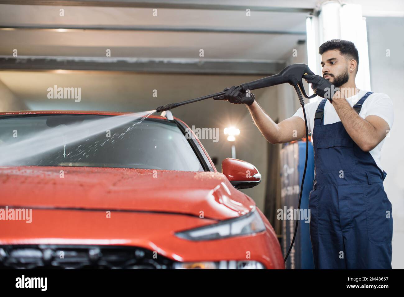 Side angle view of a man worker cleaning modern red automobile hood ...