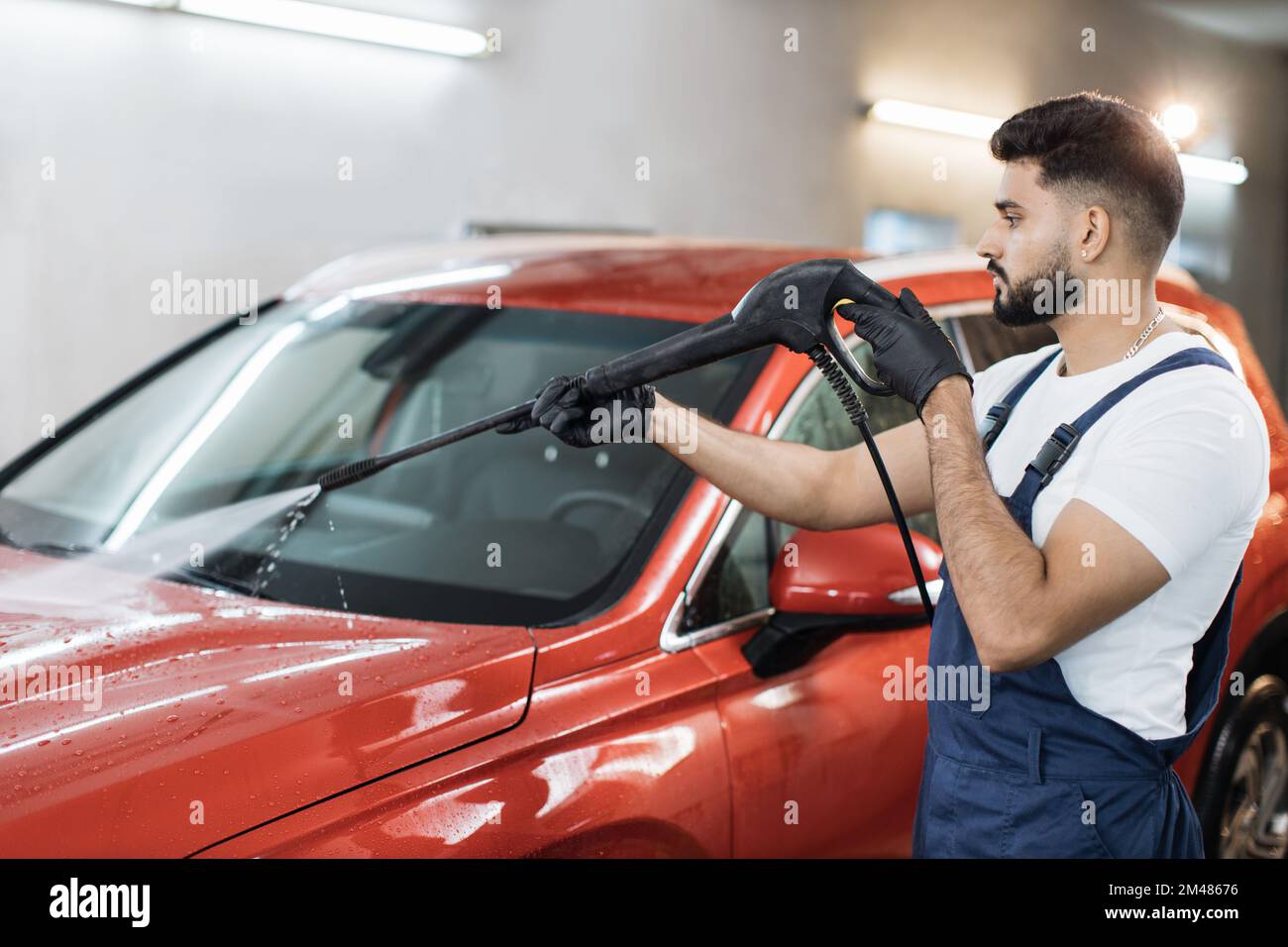 Side angle view of a man worker cleaning modern red automobile hood ...