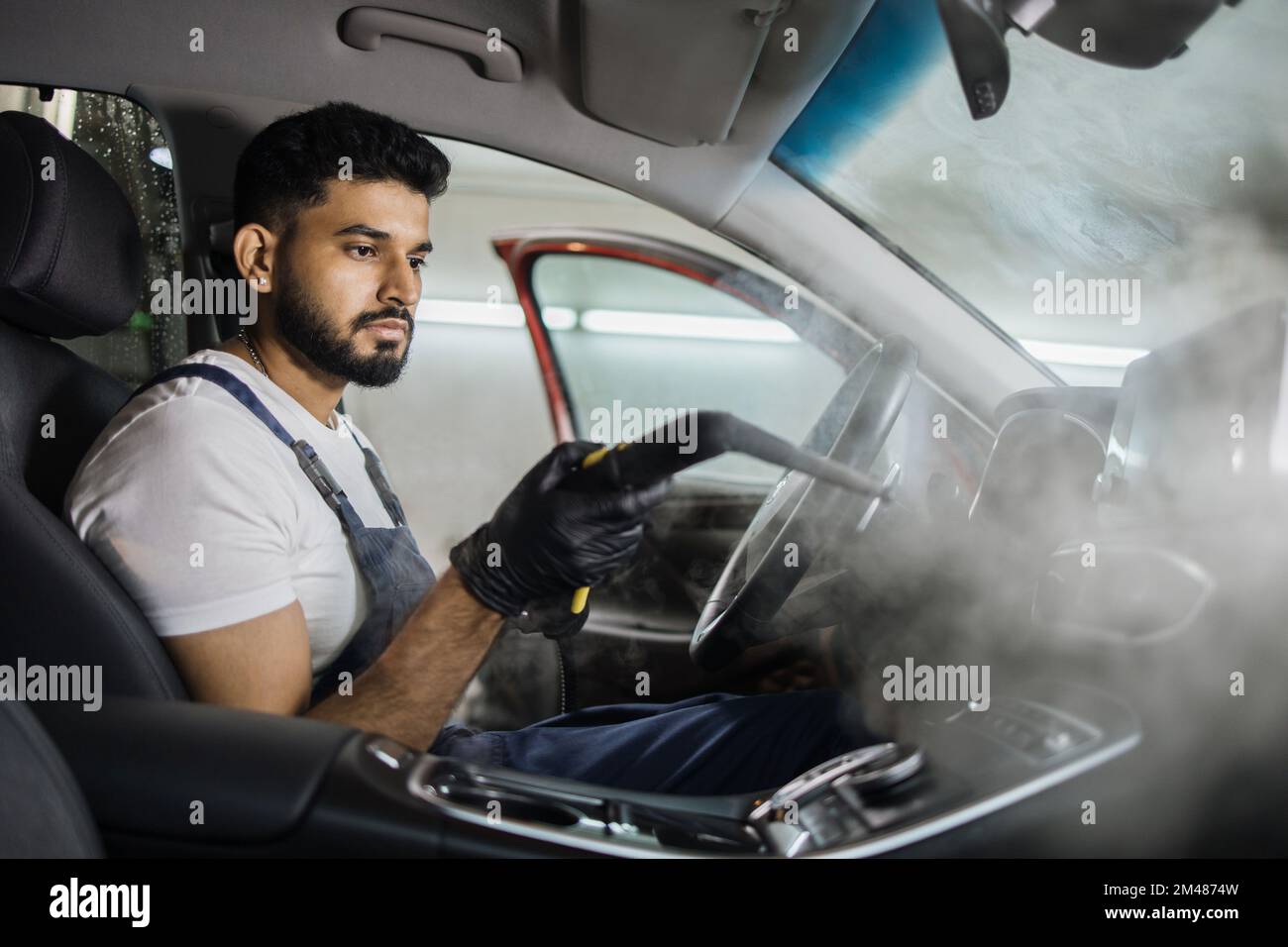 Car detailing, steam cleaning concept. Handsome man in overalls, worker ...
