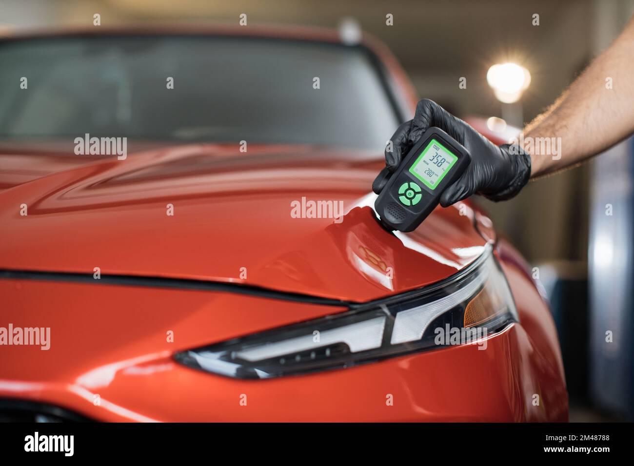 Inspector measuring paint cover thickness of red car body at the ...