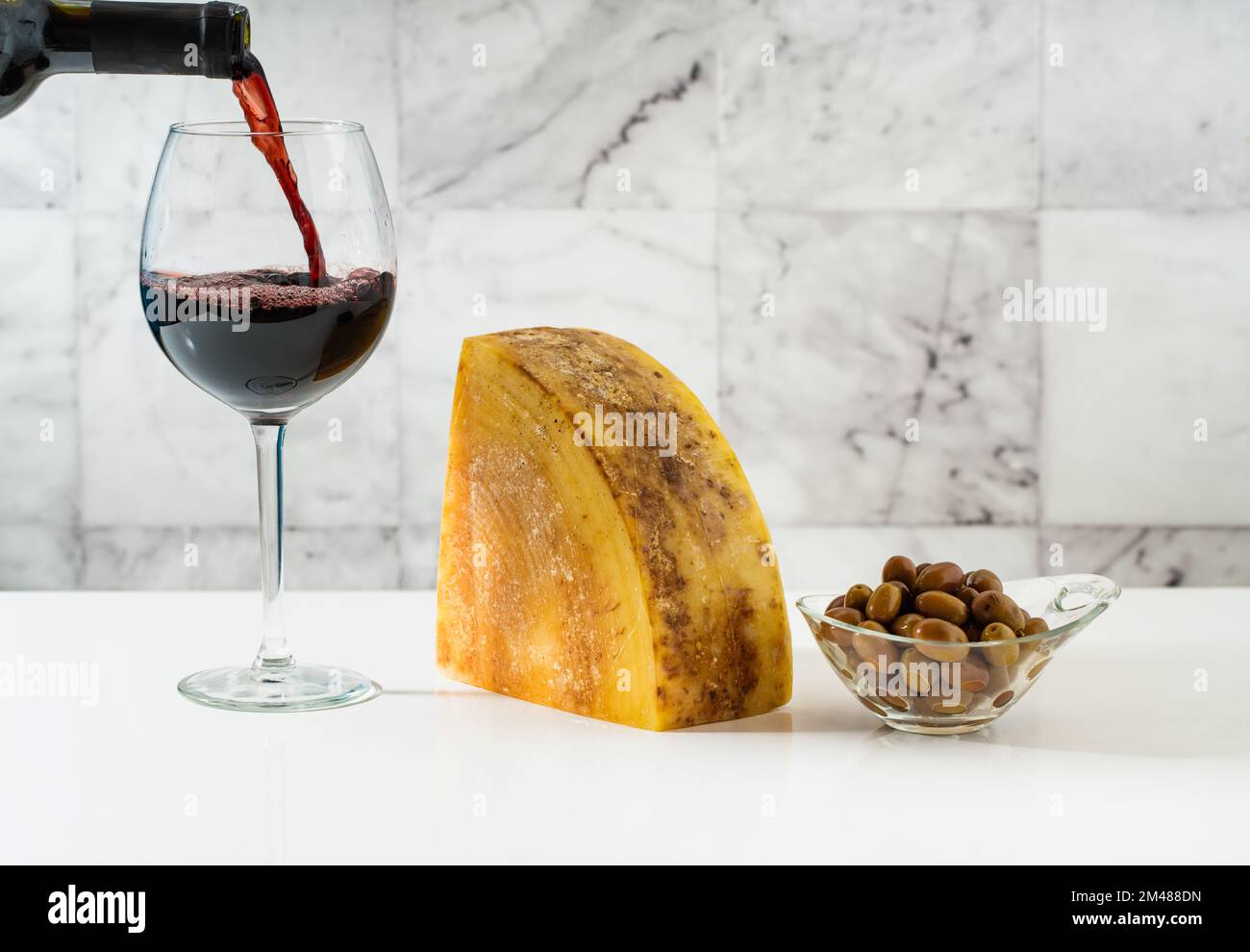 a piece of parmesan or pecorino cheese on a white table and red wine in ...