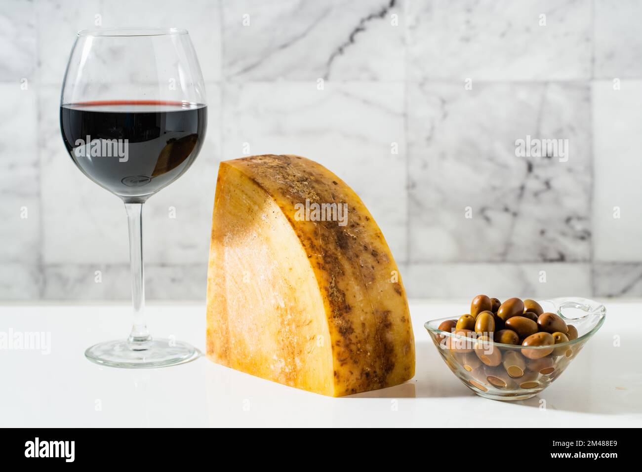 a piece of parmesan or pecorino cheese on a white table and red wine in ...
