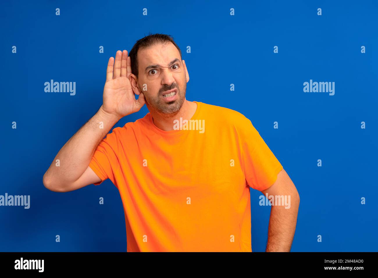 Listening man holds his hand near his ear on a blue background ...