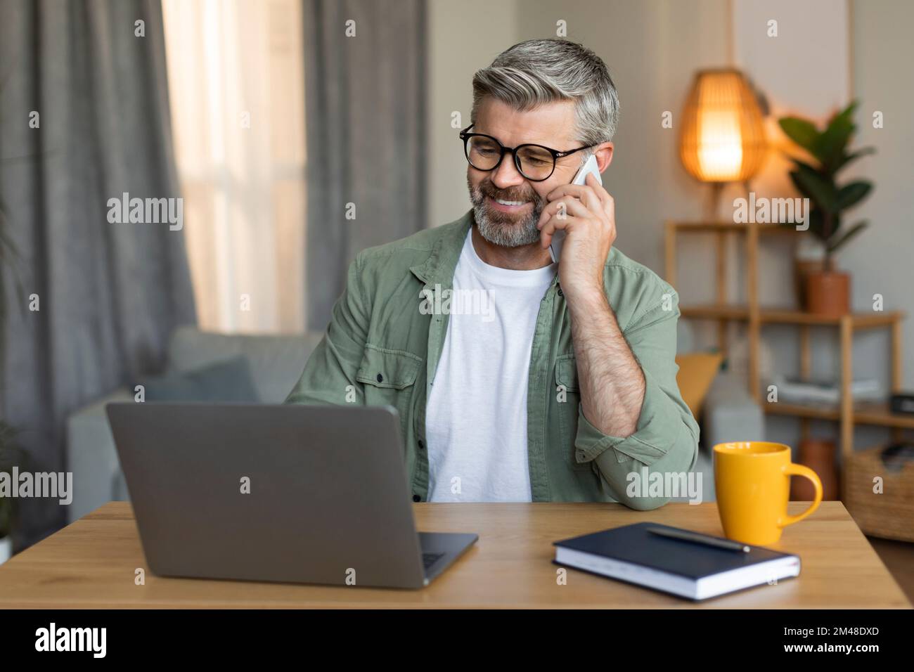 Smiling handsome old caucasian male manager calls by phone, sits at ...
