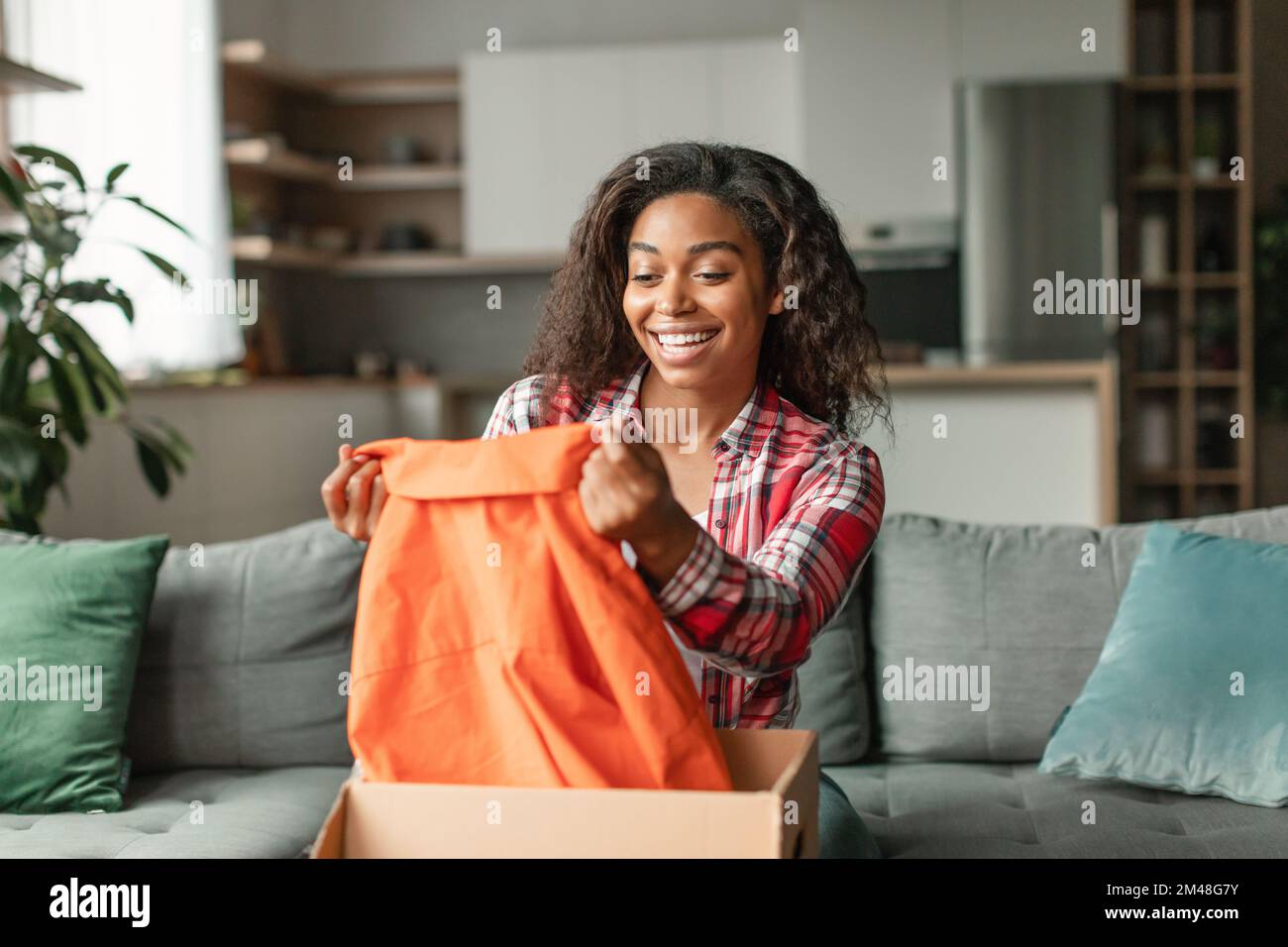 Satisfied pretty millennial black female buyer unpacking cardboard box ...