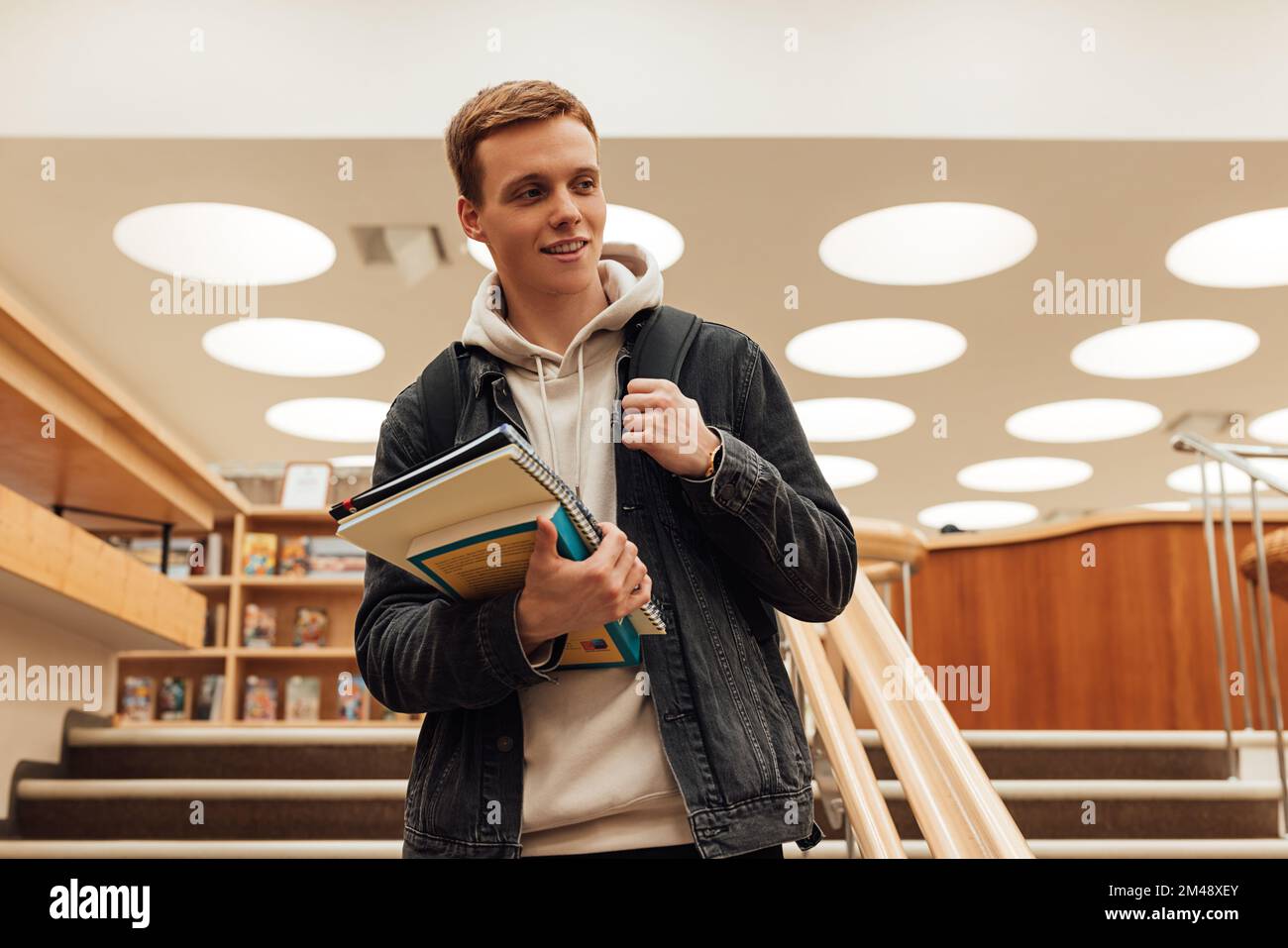 Teenager holding a books standing in college library Stock Photo - Alamy