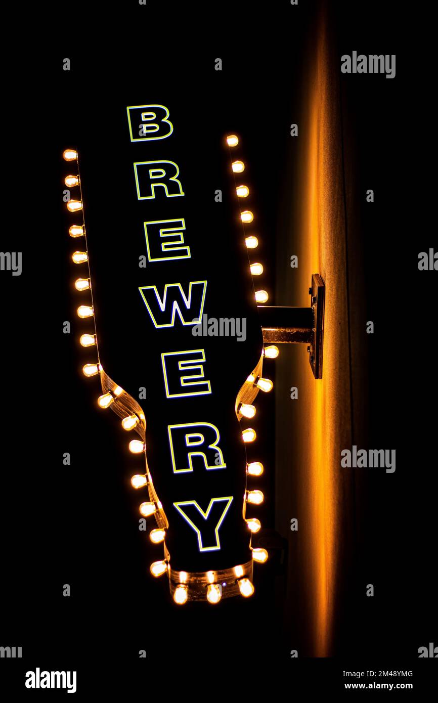 A lit brewery sign attached to a wall isolated on a dark background ...
