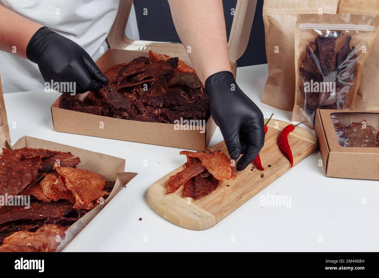 a guy puts dried meat in paper boxes in black gloves. High quality ...