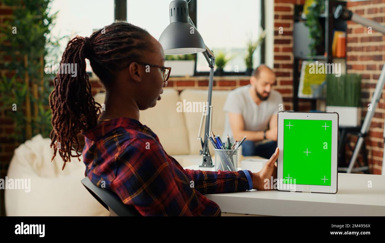 Female freelancer looking at digital tablet showing greenscreen at home ...