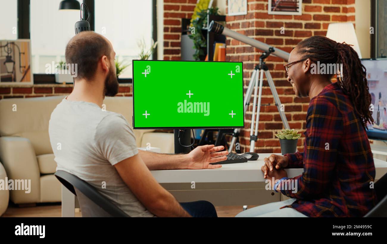 Diverse team of colleagues looking at computer with greenscreen ...