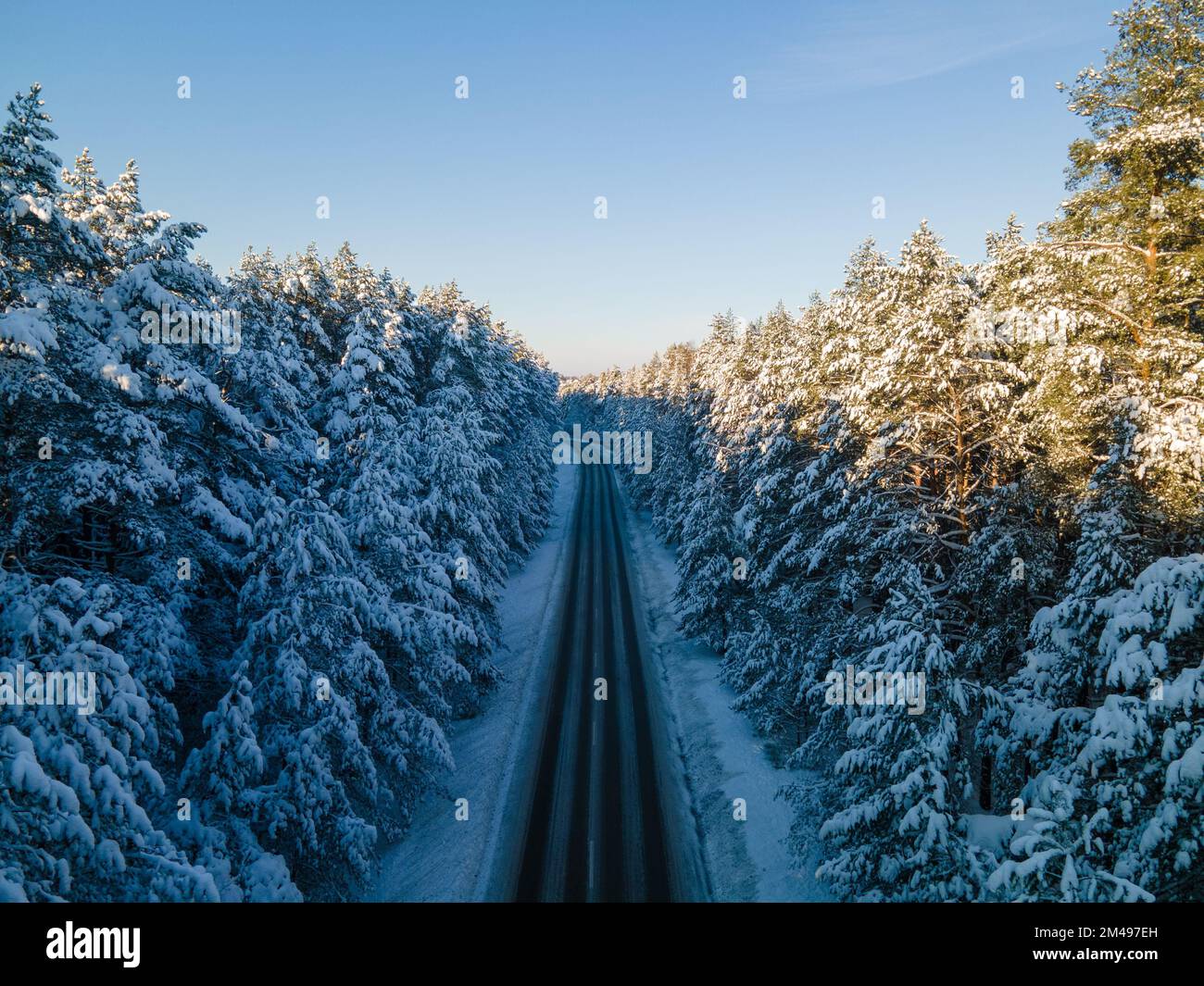 A drone shot of an asphalt road passing through a lush and snow-covered ...
