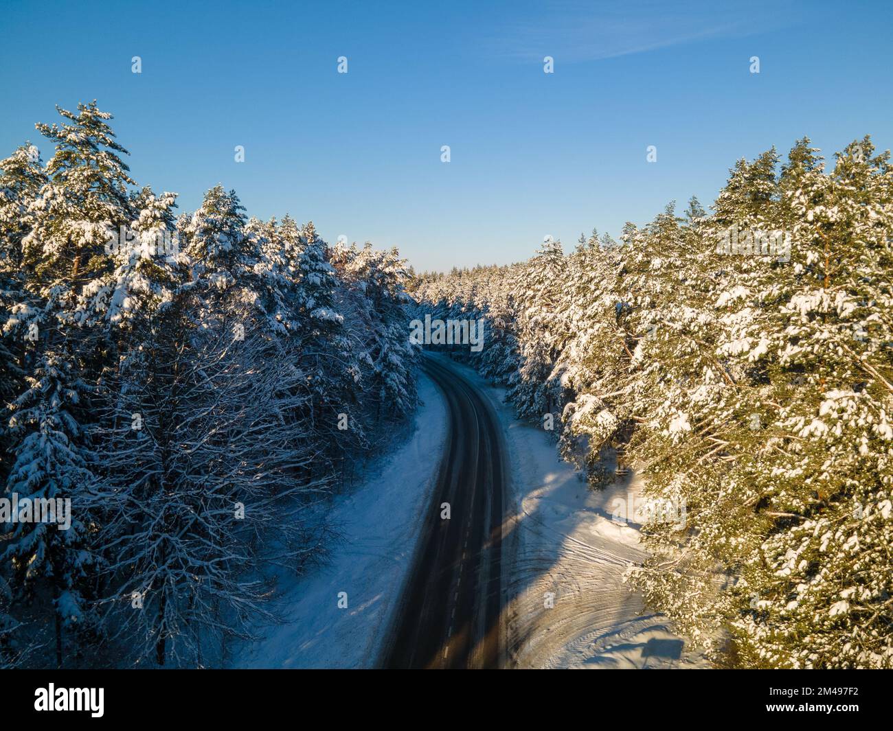 A drone shot of an asphalt road passing through a lush and snow-covered ...