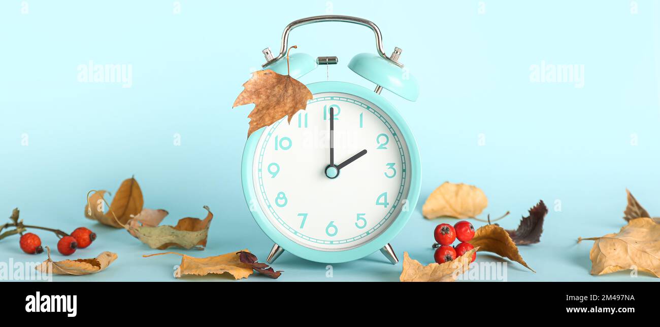 Alarm clock and autumn leaves on light blue background. Daylight saving ...