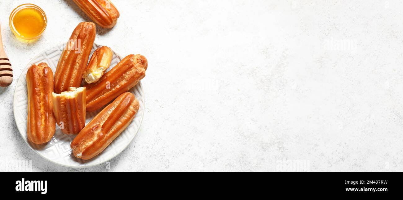 Plate of sweet eclairs and honey on light background with space for ...