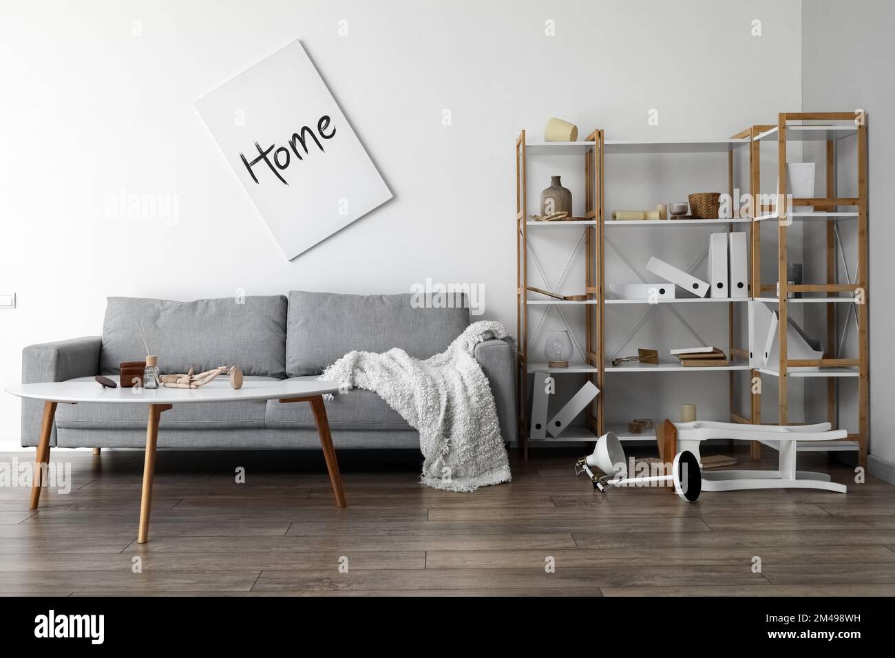 Interior of messy living room with grey sofa, tables and shelving unit ...