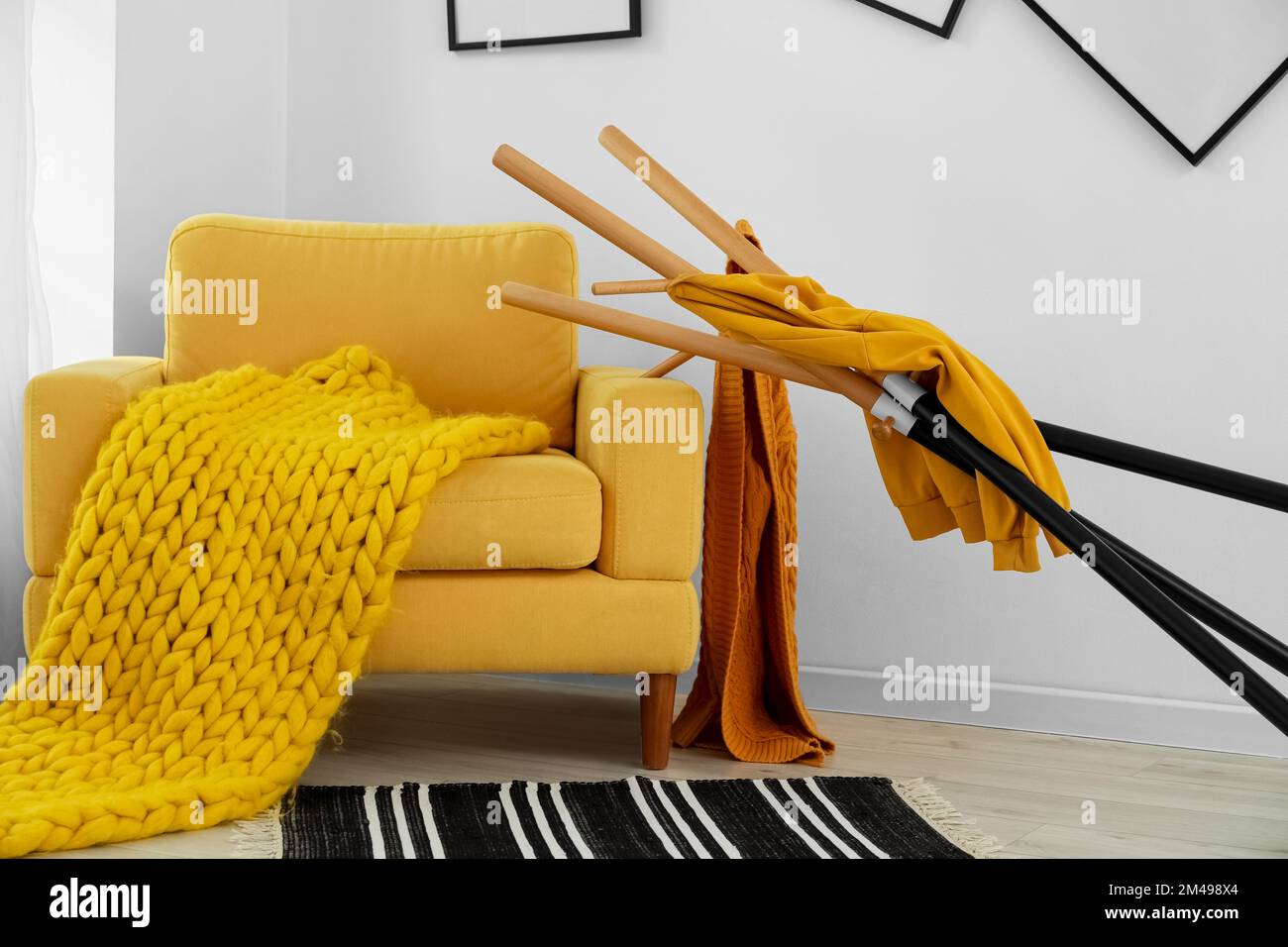 Yellow armchair with plaid and fallen clothes stand near light wall ...