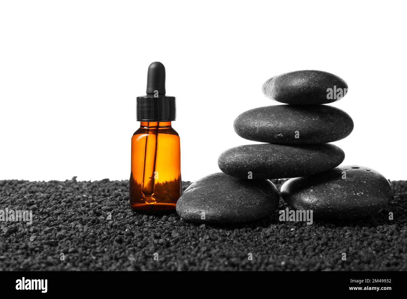 Cosmetic dropper bottle with spa stones on sand against white ...