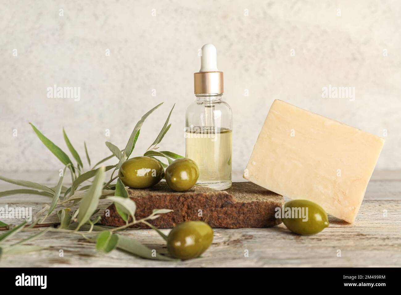 Green olives, cosmetic dropper bottle and soap bar on table near light ...