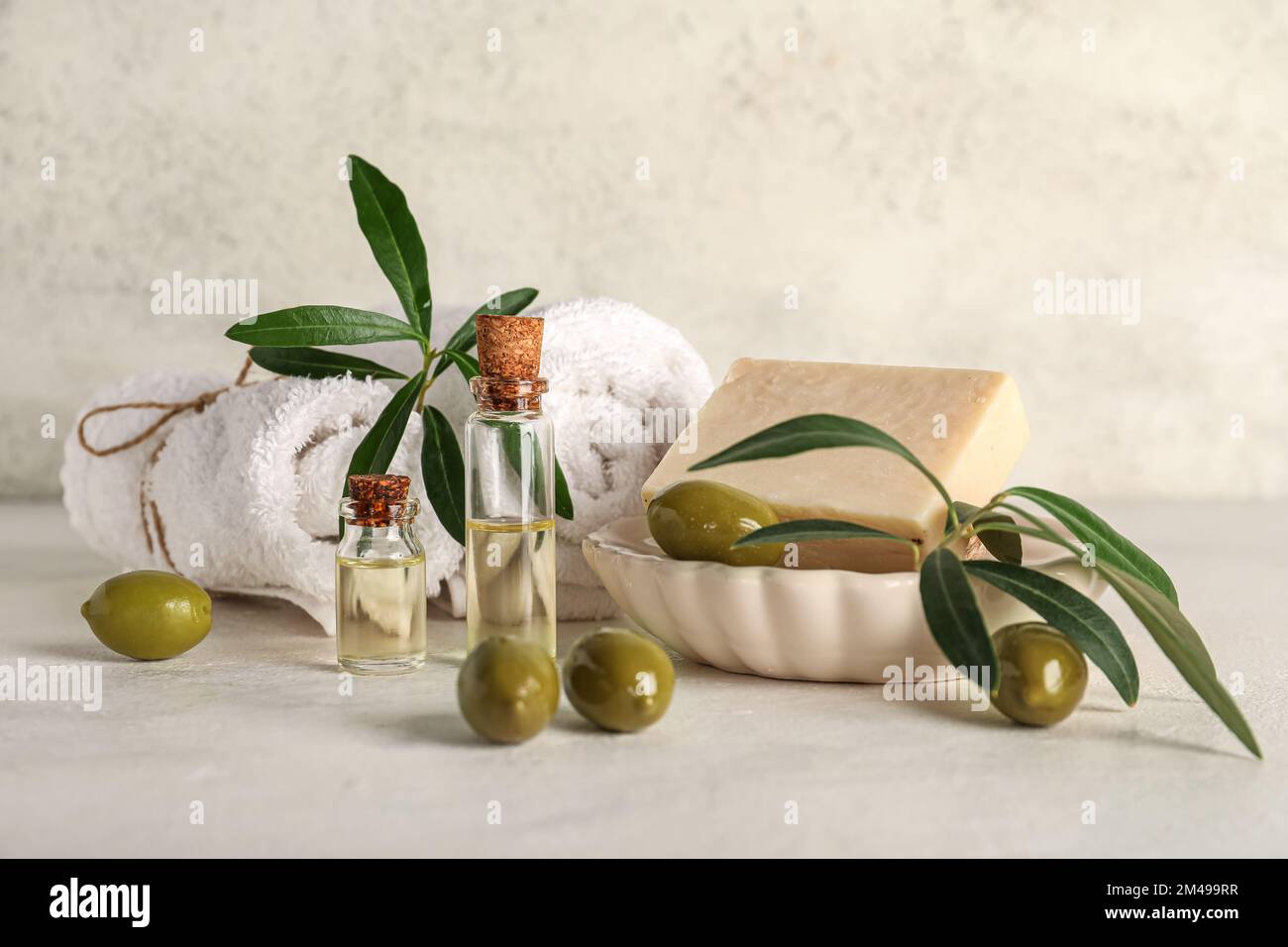Bottles of oil, green olives, soap bar and towels on light background ...