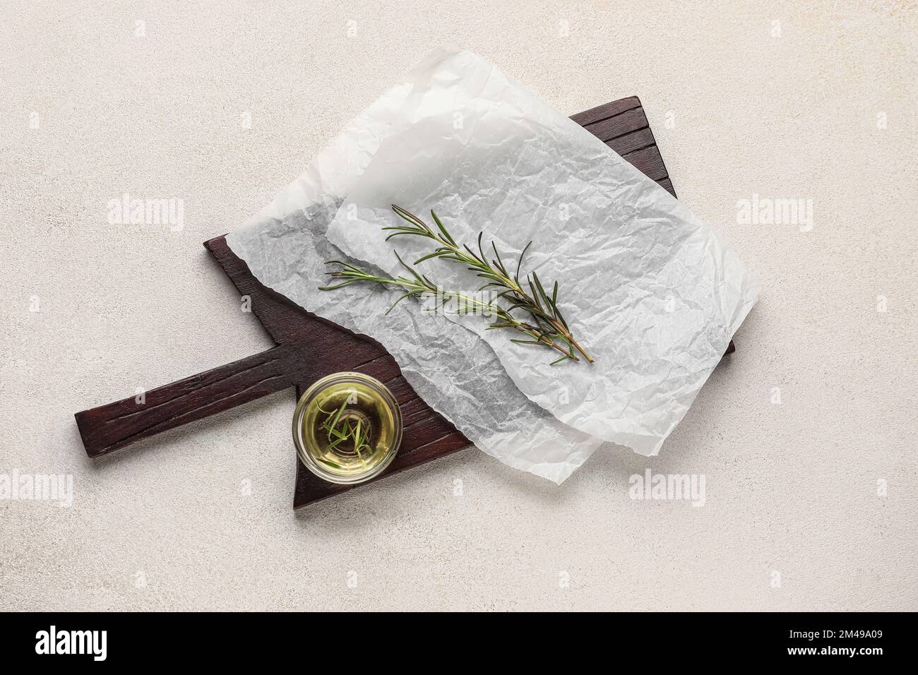 Board with baking paper, rosemary and bowl of oil on light background ...