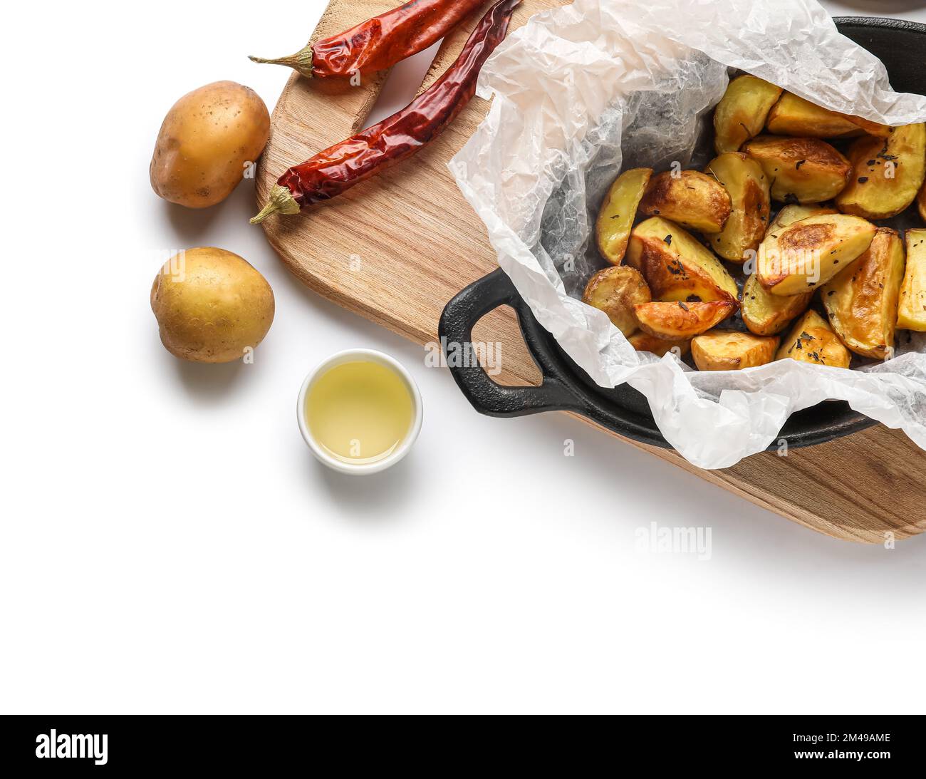 Wooden board with frying pan of tasty baked potato on white background ...