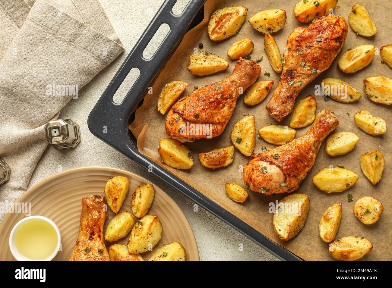 Baking sheet with tasty baked potato and chicken legs on table, closeup ...
