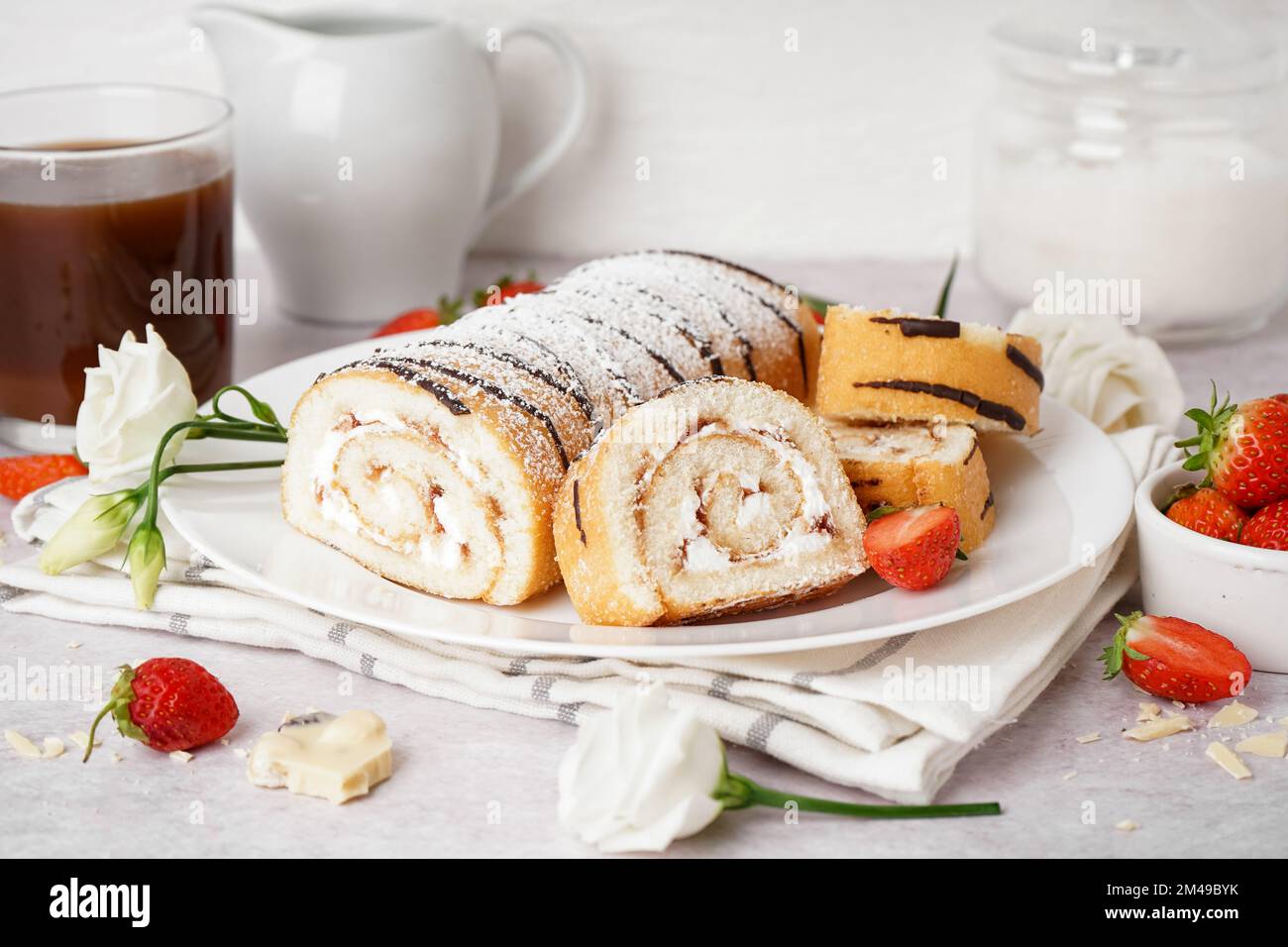 Plate with delicious sponge cake roll, fresh strawberries, floral decor ...