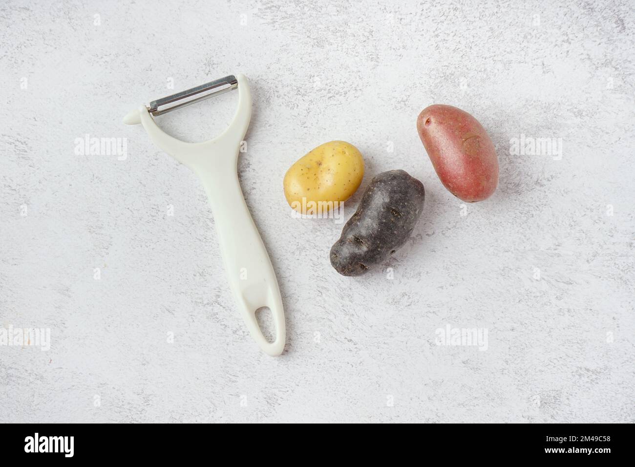 Different types of raw potatoes and peeler on light background Stock ...