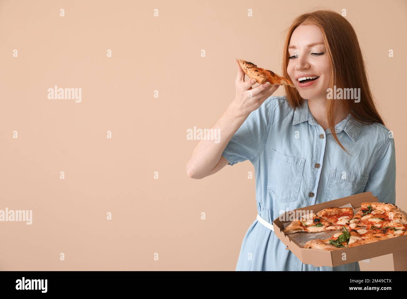Young woman eating tasty pizza on beige background Stock Photo - Alamy