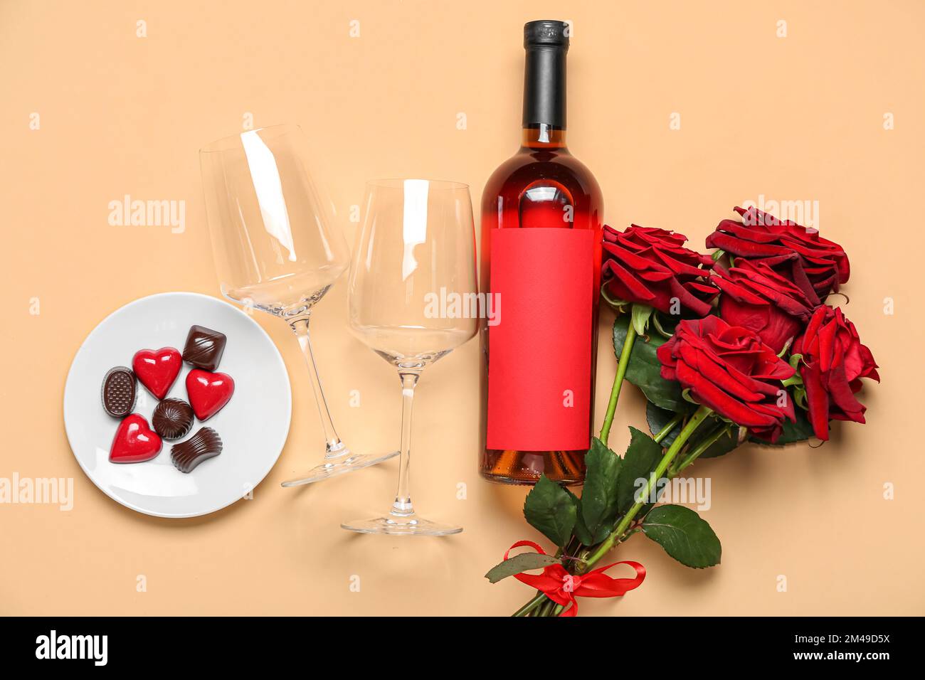 Bottle of wine, glasses, roses and candies on beige background ...