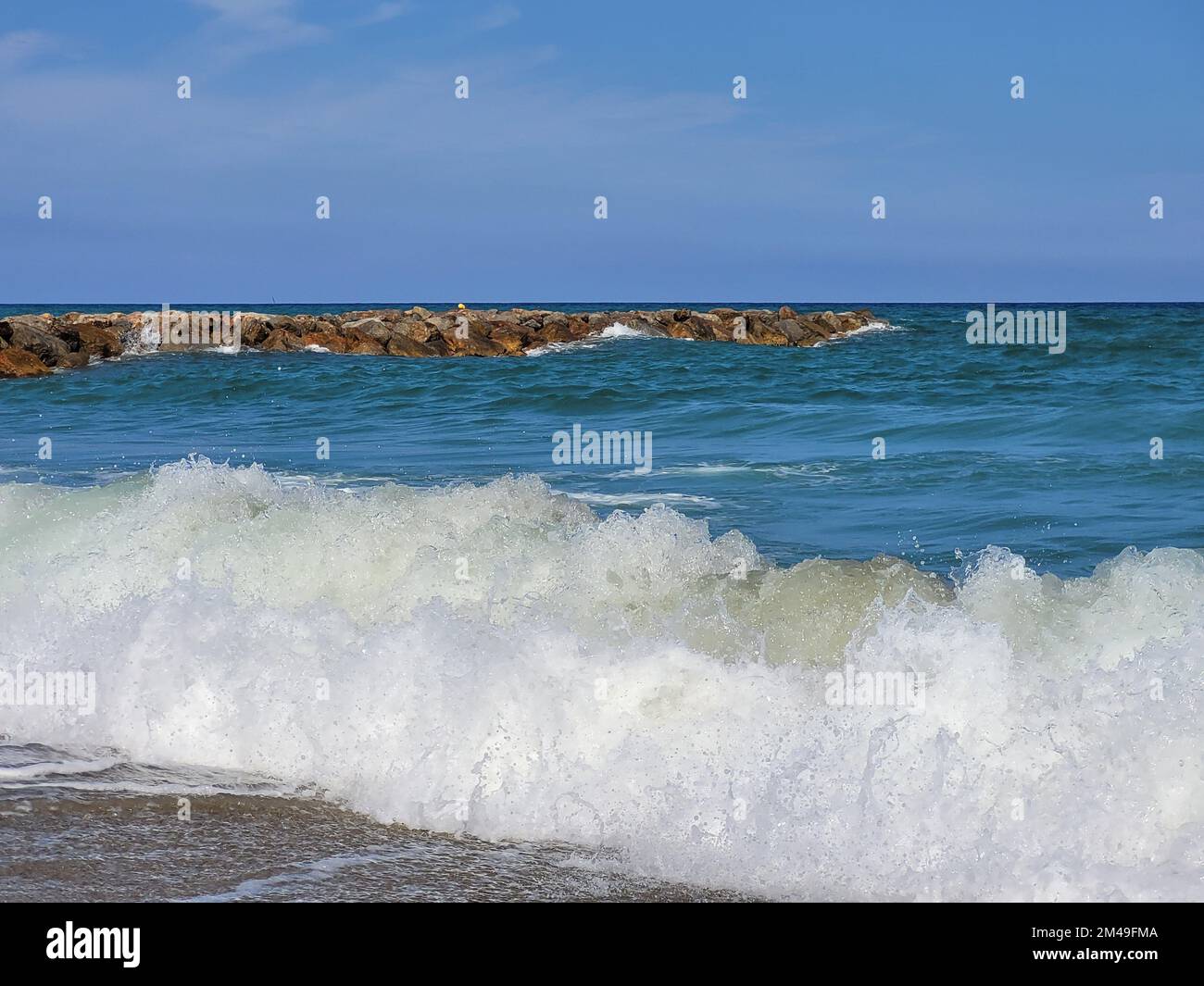 A beautiful shot from the beach of sea wave and stone barrier behind ...