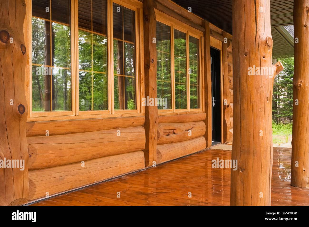 Rustic log home facade with panoramic glass pane windows and veranda ...