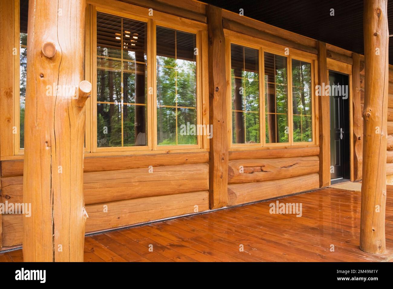 Rustic log home facade with panoramic glass pane windows and veranda ...