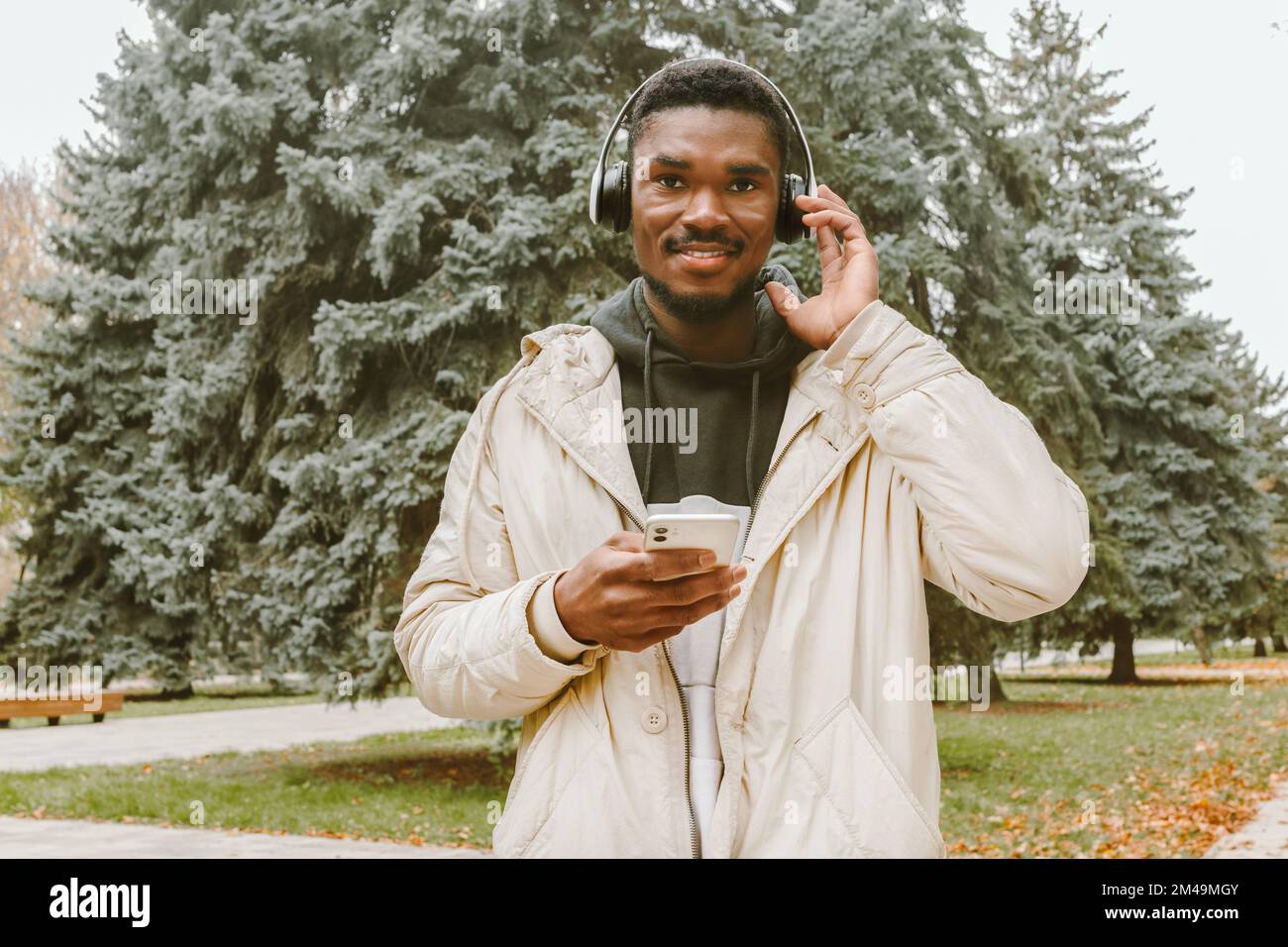 Handsome black man in wireless headphones listening music over park ...