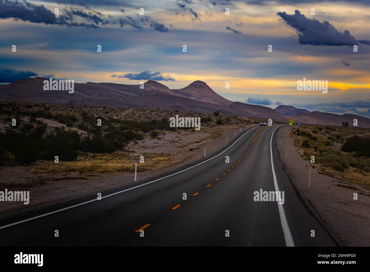 A highway going through the Arizona desert with mountains and sunset ...