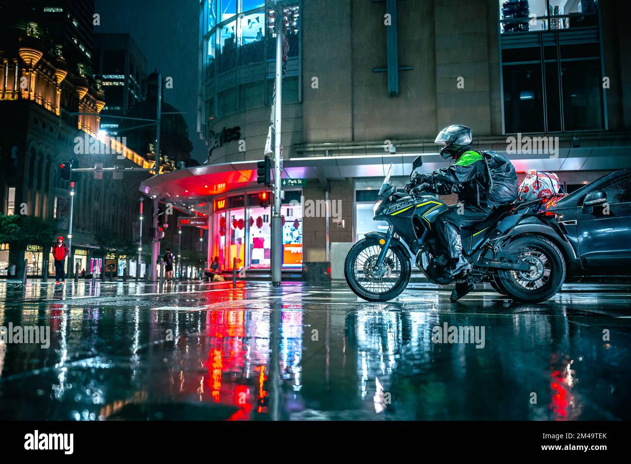 A motorcyclist stops at traffic lights on a rainy night with glowing ...