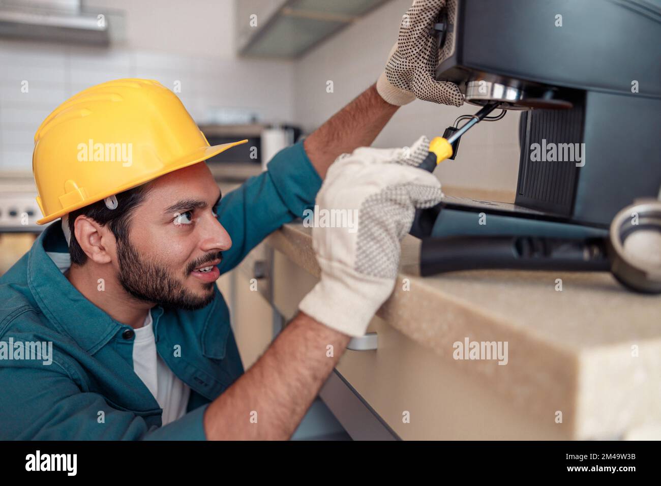 Man with screwdriver fixing coffee machine at table in kitchen ...