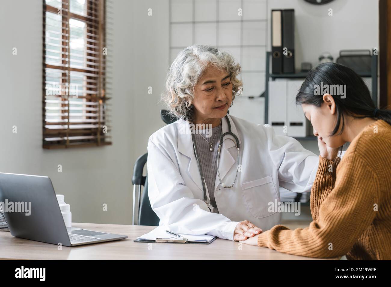 Senior doctor assisting a woman in her office. the patient is crying ...