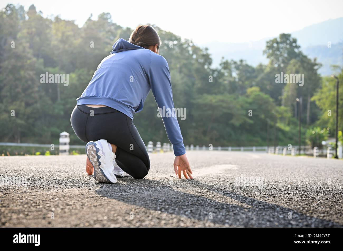 Athlete Asian female runner in comfortable sportswear in running start pose, preparing to run on ...