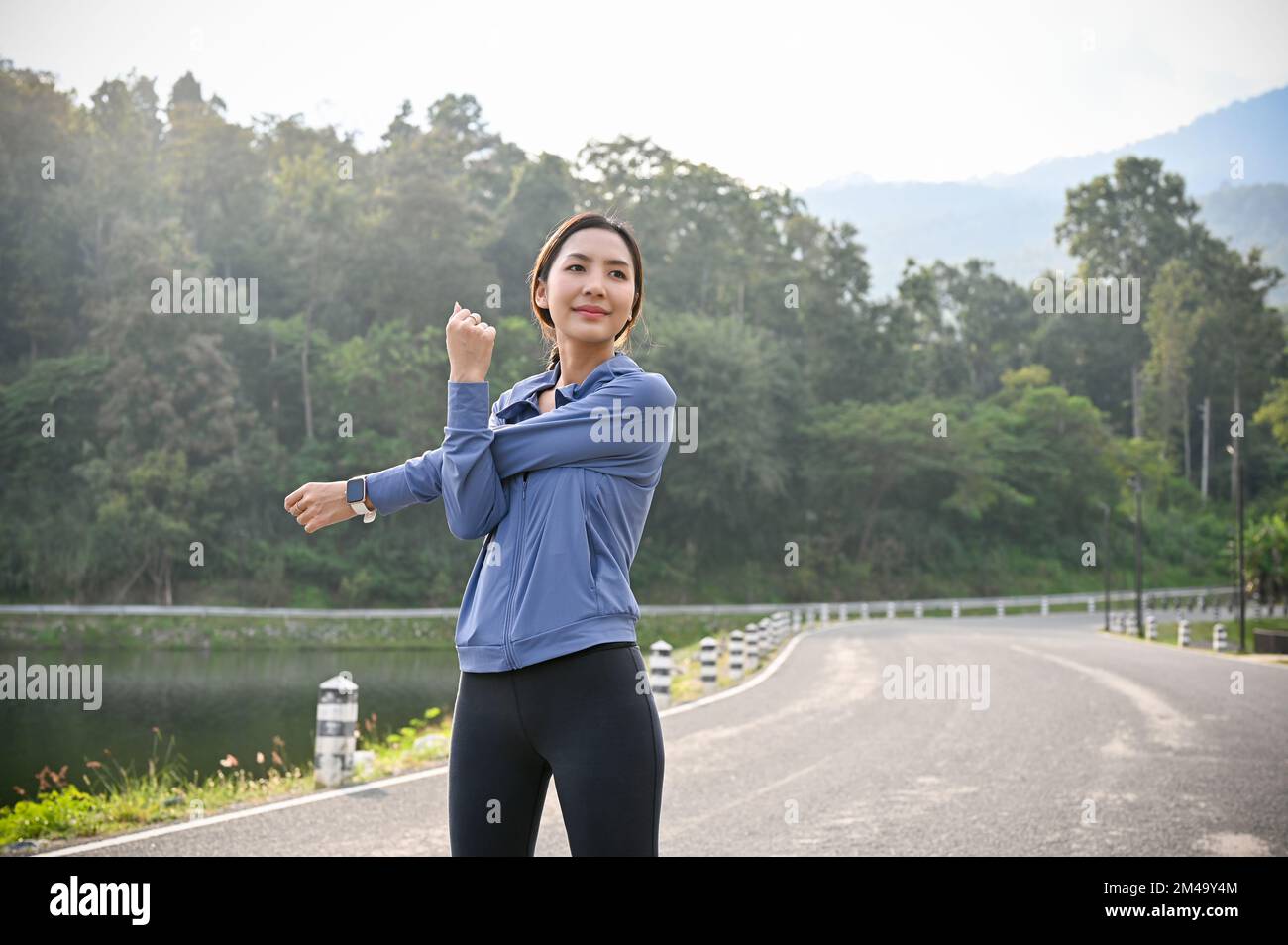 Healthy Asian woman in sportswear is stretching her arms and body before running along the ...
