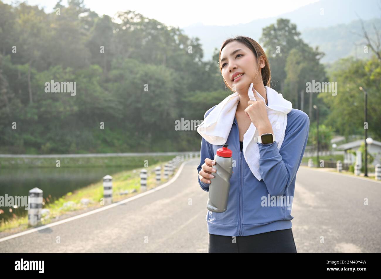 Tired and sweaty Asian woman in sportswear holding a bottle of water ...