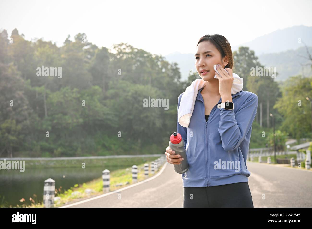 Tired and sweaty Asian woman in sportswear holding a bottle of water ...