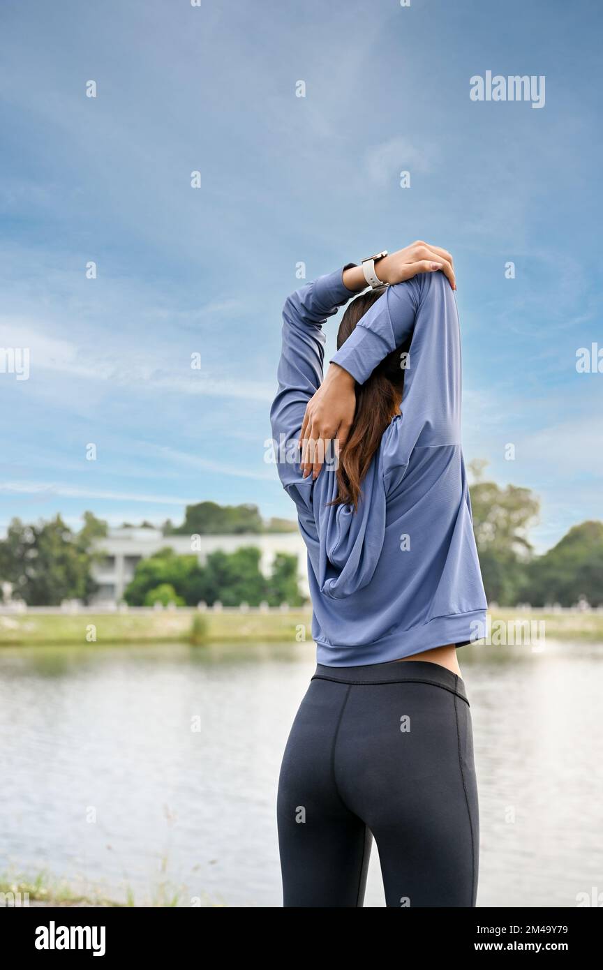 Healthy Asian woman in sportswear stretching her arms and shoulders, warming up or cooling down ...
