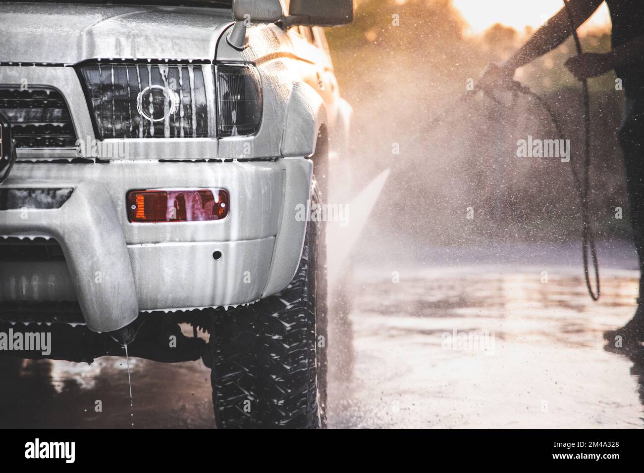 Washing white car at a self-service car wash with a high-pressure water ...