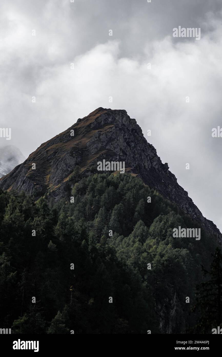 A vertical shot of a mountain covered in forests with a dramatic cloudy ...