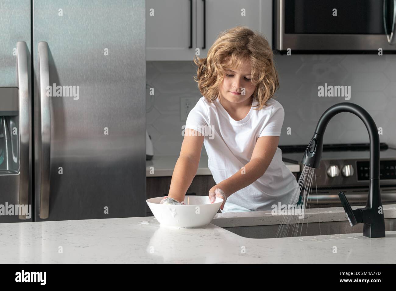 Kid boy washing dishes in the kitchen interior. Child helping his parents with housework Stock ...