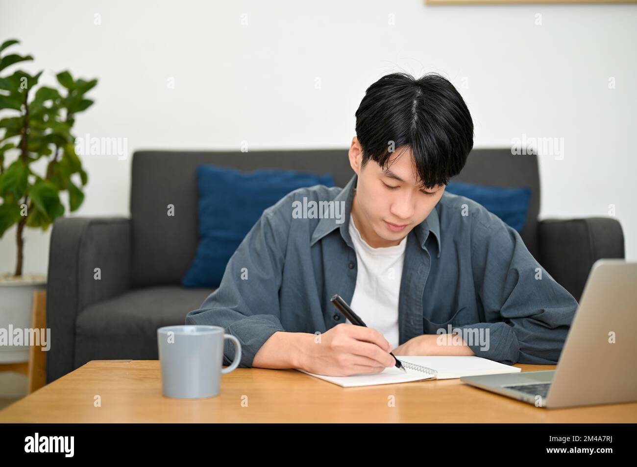 Focused young Asian male college student writing diary or taking notes ...